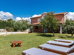 Uma villa com piscina, gramado e espreguiçadeiras.