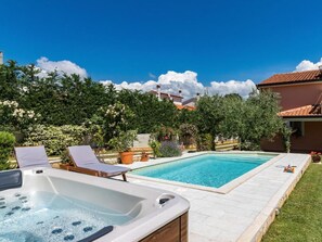 Piscina com espreguiçadeiras e uma banheira de hidromassagem em um quintal.