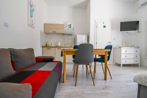Uma sala de estar moderna com um sofá, uma mesa de jantar com cadeiras, uma televisão e uma área de cozinha com armários e eletrodomésticos.