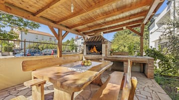 Uma pérgola de madeira ao ar livre com um forno de tijolo e uma mesa de madeira com bancos.