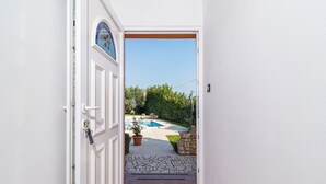 Uma porta de entrada para um quintal com piscina, vasos de plantas e um muro de pedra.