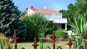 Uma casa com telhado de telhas vermelhas, rodeada por vegetação e árvores.