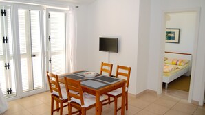 Uma sala de jantar com mesa e cadeiras, uma televisão na parede e uma cama no quarto vizinho.