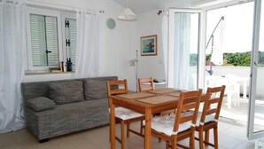Quarto com sofá, mesa de jantar de madeira, cadeiras, luminária e janela com cortinas.