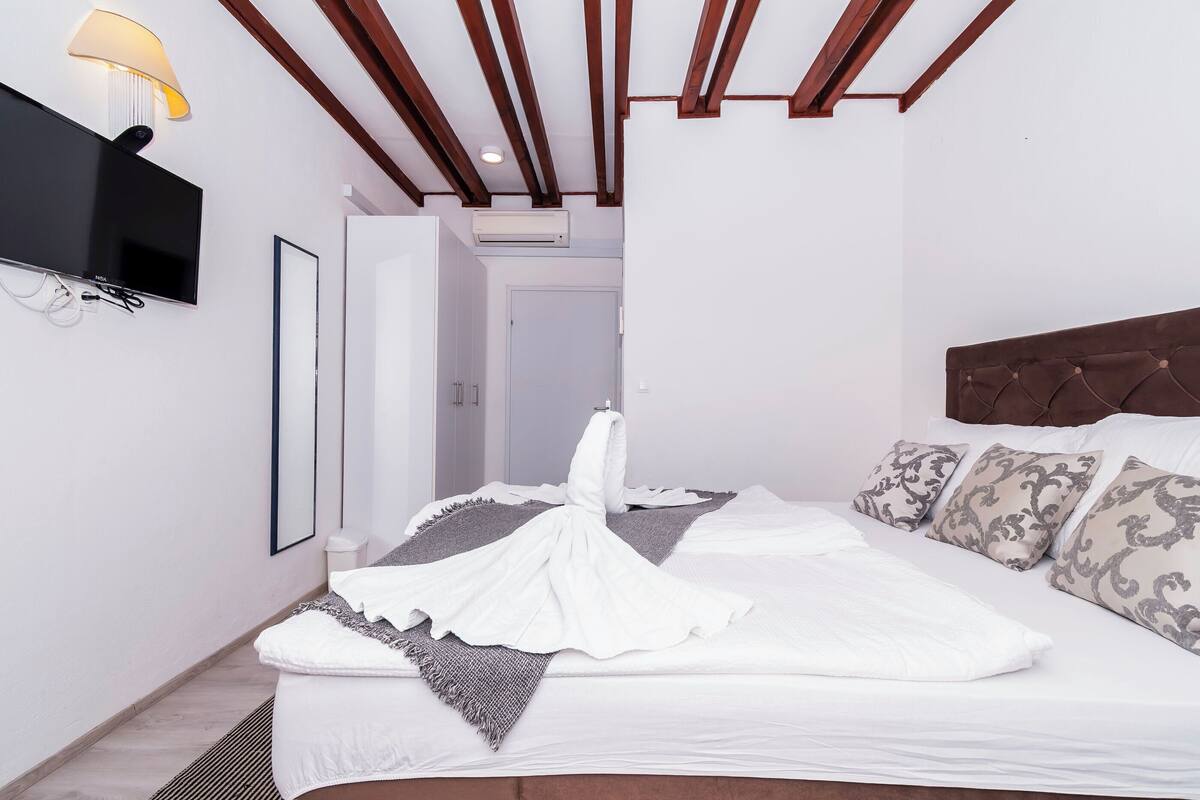Quarto com cama, televisão na parede e ventoinha no teto.