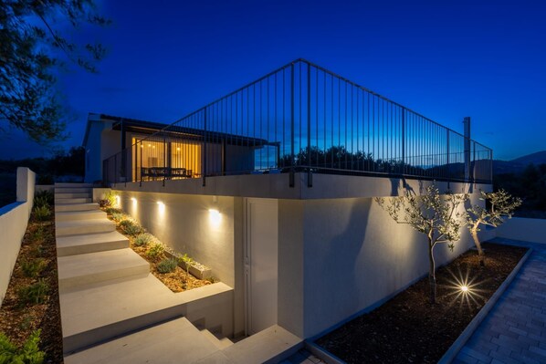 Uma casa moderna com telhado plano, grandes janelas e uma escadaria que leva à entrada.