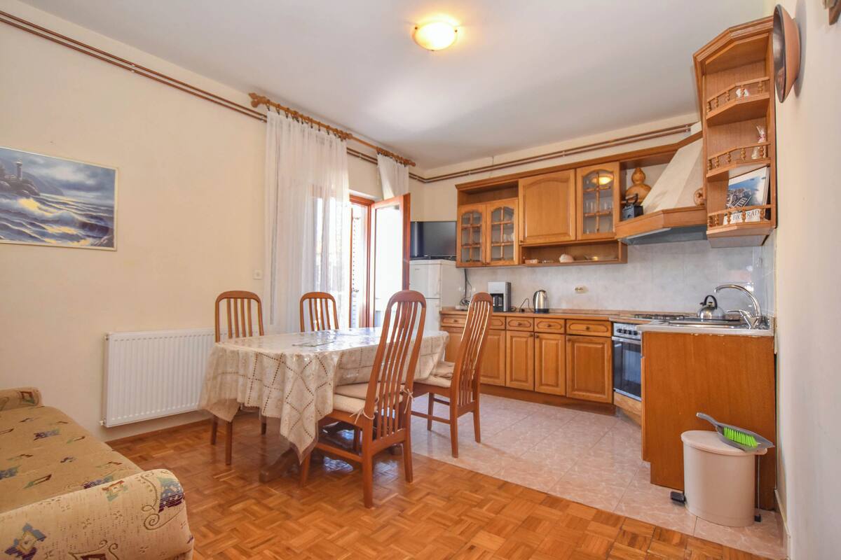 Uma sala de jantar com mesa e cadeiras, uma cozinha com armários de madeira e eletrodomésticos, e um radiador na parede.