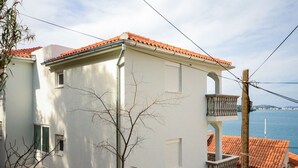 Um edifício branco com telhado de telhas vermelhas, varanda e vista para o mar.