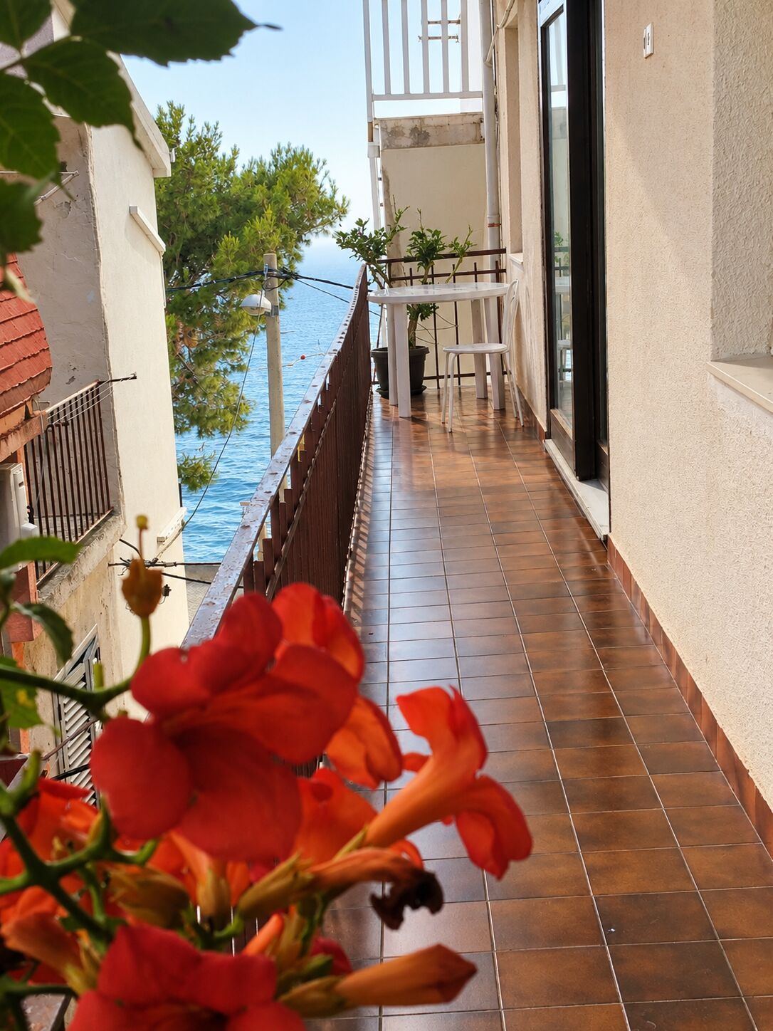 Uma varanda com vista para o mar, uma mesa e cadeiras.