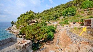 Um imóvel costeiro com um caminho de pedra que leva a um edifício rústico, rodeado por vegetação exuberante e com vista para o mar.