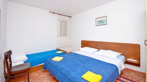 Quarto com duas camas, uma cadeira e uma mesinha.