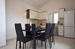 Uma cozinha moderna com armários brancos, uma mesa de jantar preta com quatro cadeiras e uma geladeira branca.