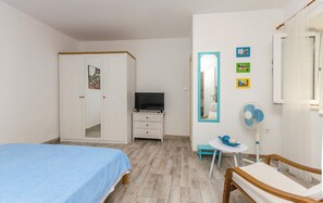 Quarto com cama, televisão, guarda-roupa, espelho e ventilador.