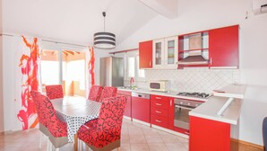 Uma cozinha moderna com armários vermelhos, uma mesa de jantar com cadeiras estampadas e um fogão à vista.