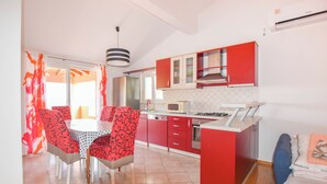Cozinha moderna com armários vermelhos, bancada branca e área de refeições com cadeiras estampadas.