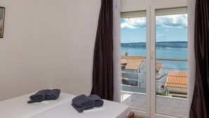 Quarto com uma cama, duas toalhas e vista para o mar através de uma porta de vidro.