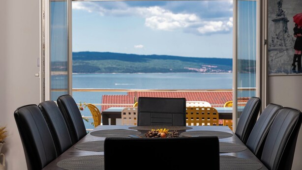 Uma sala de jantar com uma mesa posta para seis pessoas, com vista para o mar e colinas.