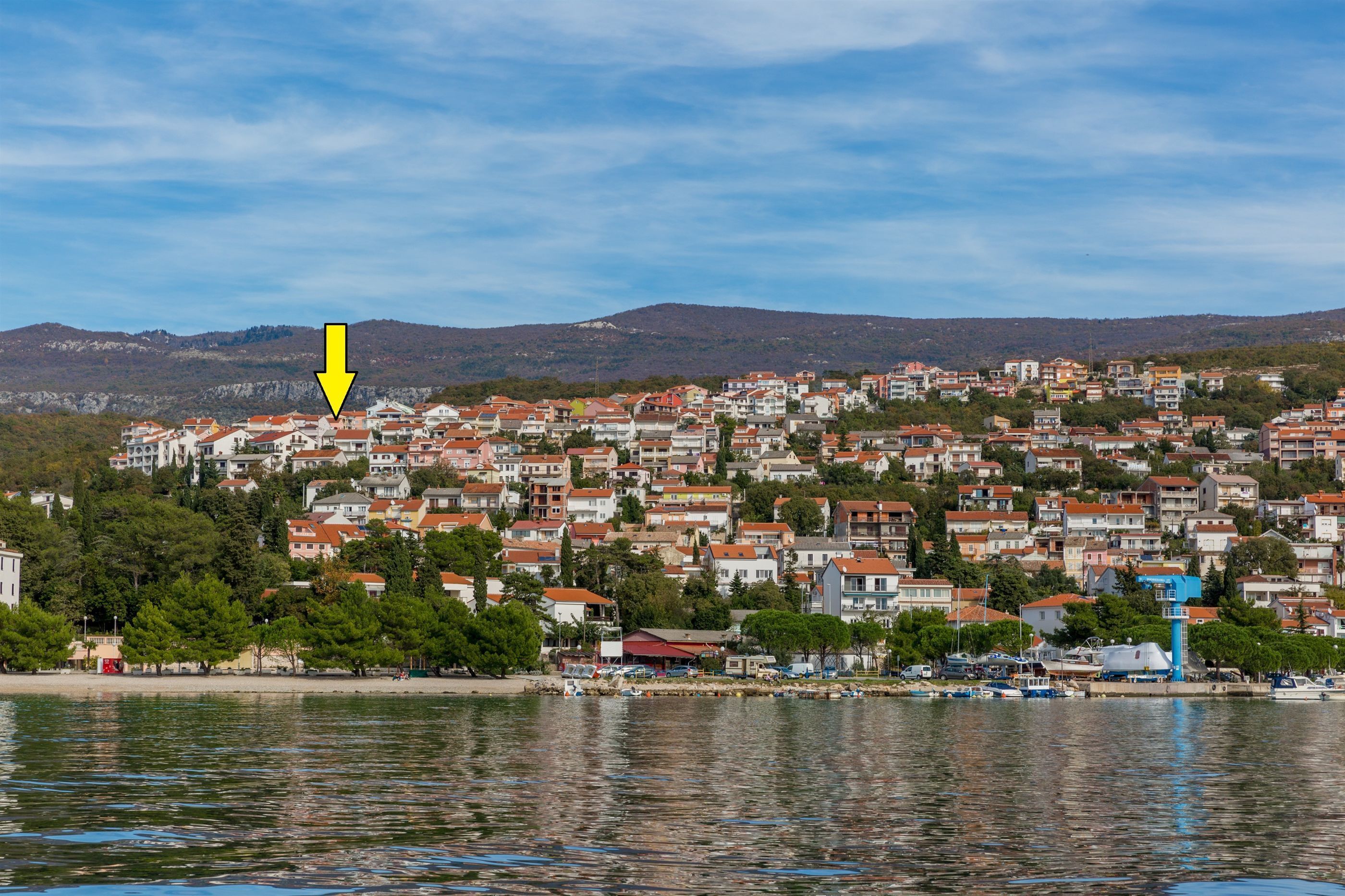 Uma vila costeira com um conjunto denso de edifícios, um corpo de água em primeiro plano e montanhas ao fundo.