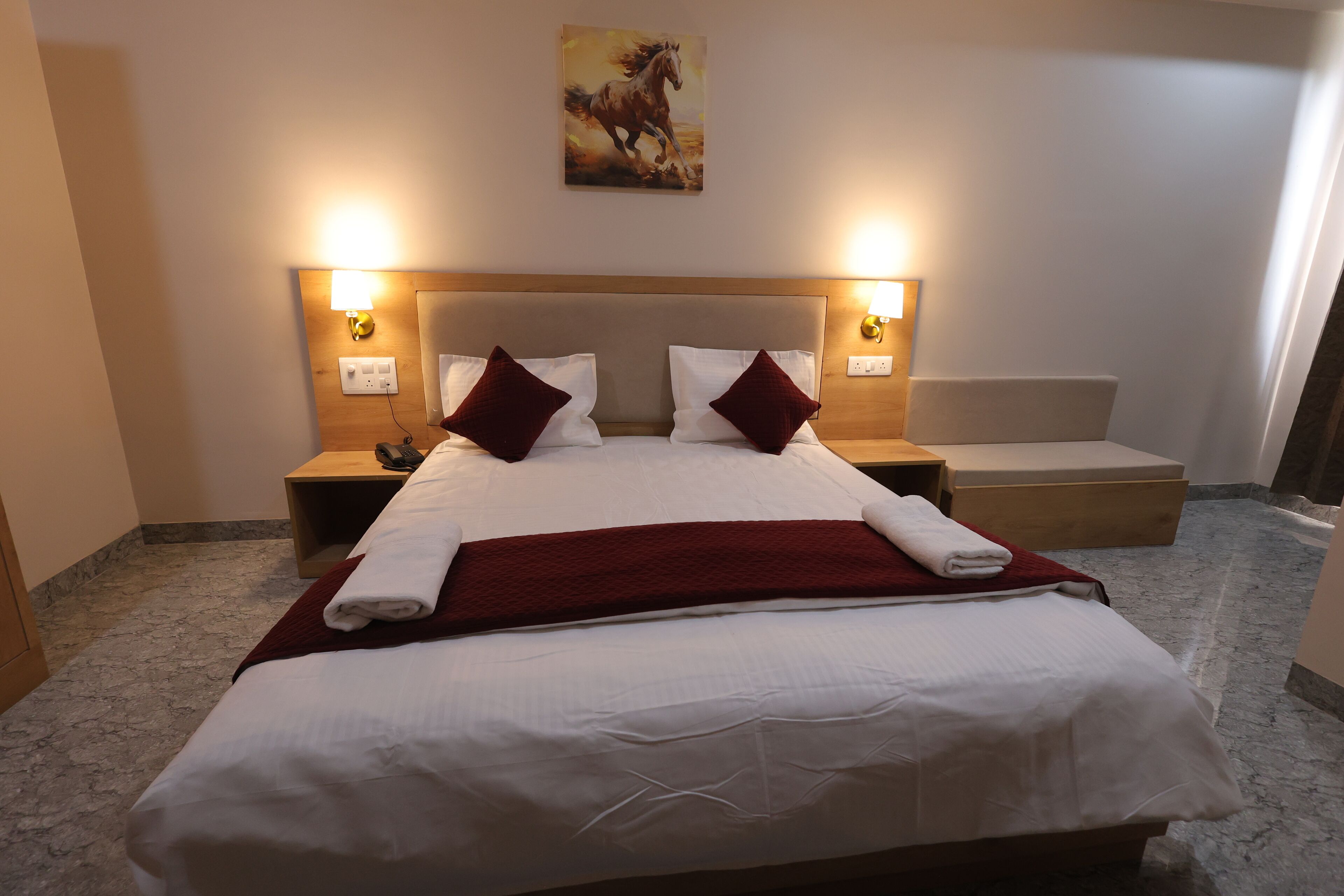 Uma cama bem arrumada com roupa de cama branca e vermelha, duas luminárias de cabeceira, um painel de madeira e um quadro acima da cama.