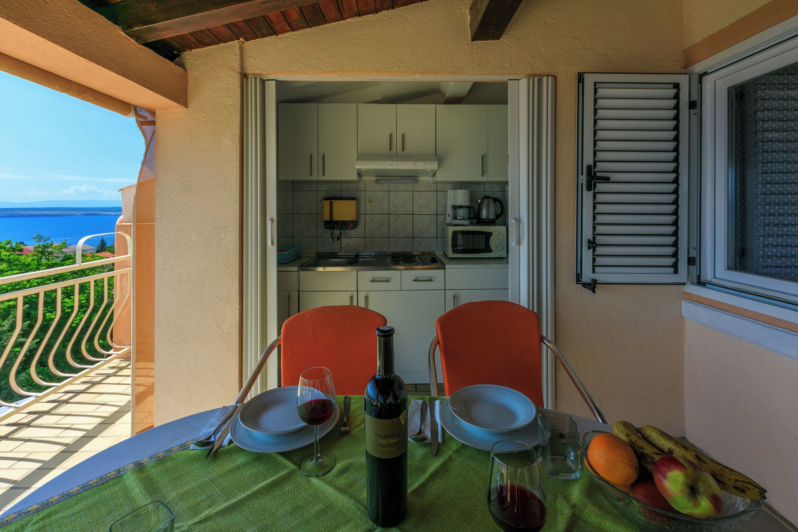 Varanda com uma mesa posta para dois, uma garrafa de vinho e uma tigela de frutas.