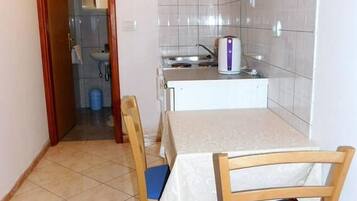 Cozinha compacta com mesa e cadeiras, armário branco sobre a pia e painel de azulejos.