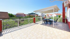 Uma varanda com mesa e cadeiras, guarda-corpo branco e vista do bairro ao redor.