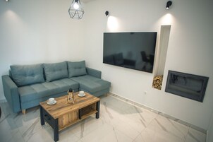 Uma sala de estar moderna com um sofá azul-turquesa, uma mesa de centro de madeira com duas xícaras e um candeeiro, uma televisão de tela plana na parede e uma lareira com lenha.