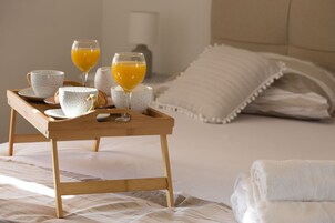 Cama arrumada com uma bandeja de madeira contendo itens de café da manhã, como croissants e suco de laranja, em um quarto de hotel.