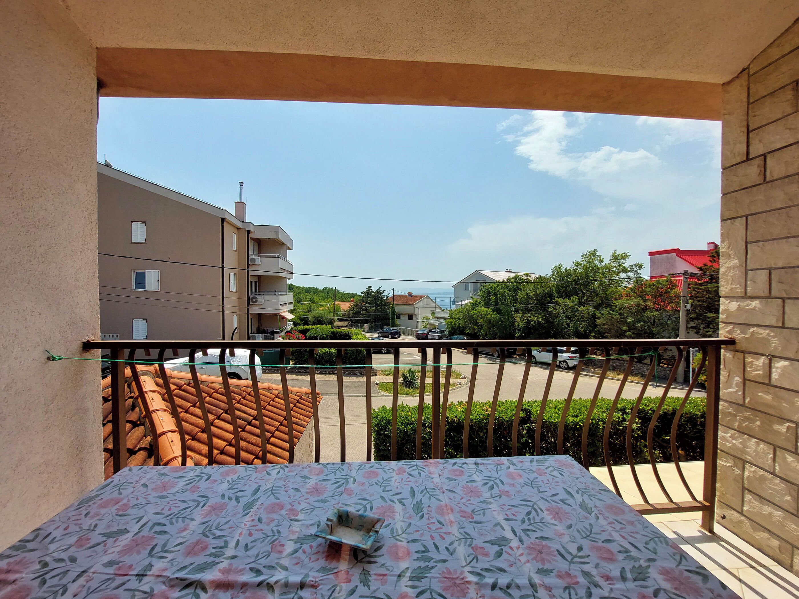 Uma varanda com uma mesa, vista para a rua e edifícios ao fundo.