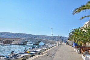 Marina costeira com barcos atracados, uma passarela para pedestres e uma ponte ao fundo.