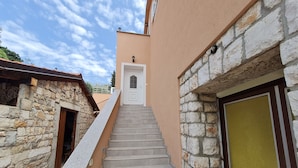 Uma escadaria leva a uma porta, com uma parede de pedra de um lado e uma parede bege do outro.