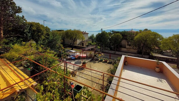 Zona residencial com vista para o mar, um jardim com plantas em vasos e um edifício com telhado de azulejos.