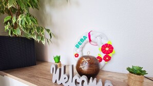 Um balcão de recepção de madeira com uma placa de 'Welcome', um enfeite de parede com 'BEBA' e flores, e duas pequenas plantas em vasos.