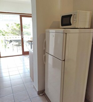 Uma cozinha com geladeira branca, micro-ondas em cima e porta de vidro corrediça que dá para uma área externa com cadeiras e mesa.
