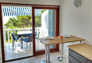 Quarto com porta de vidro deslizante que dá para um pátio externo com mesa e cadeiras, um banco de madeira e uma pequena mesa com uma tigela de frutas e um copo.