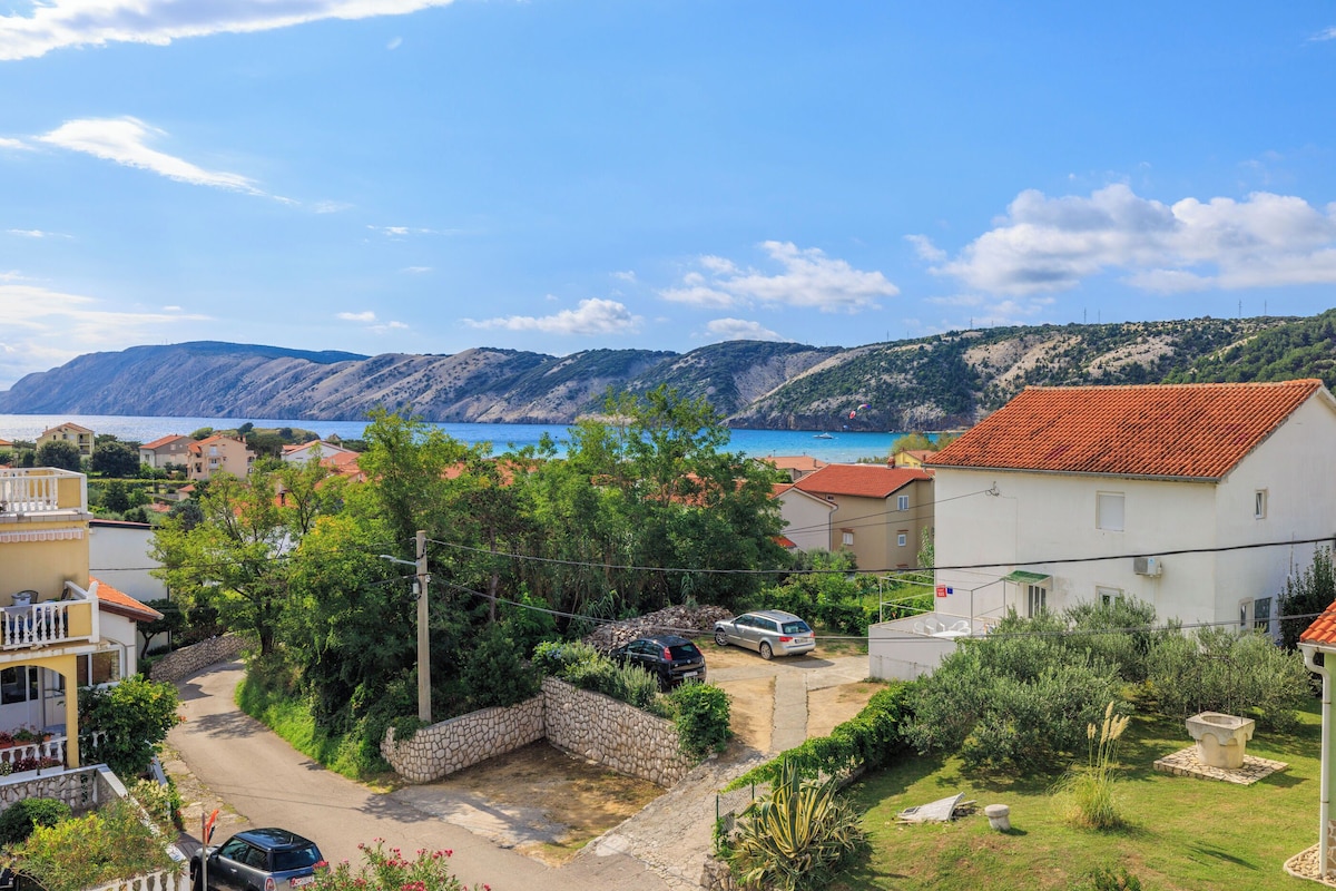 Uma área residencial com casas, um muro de pedra e vista clara para o mar.