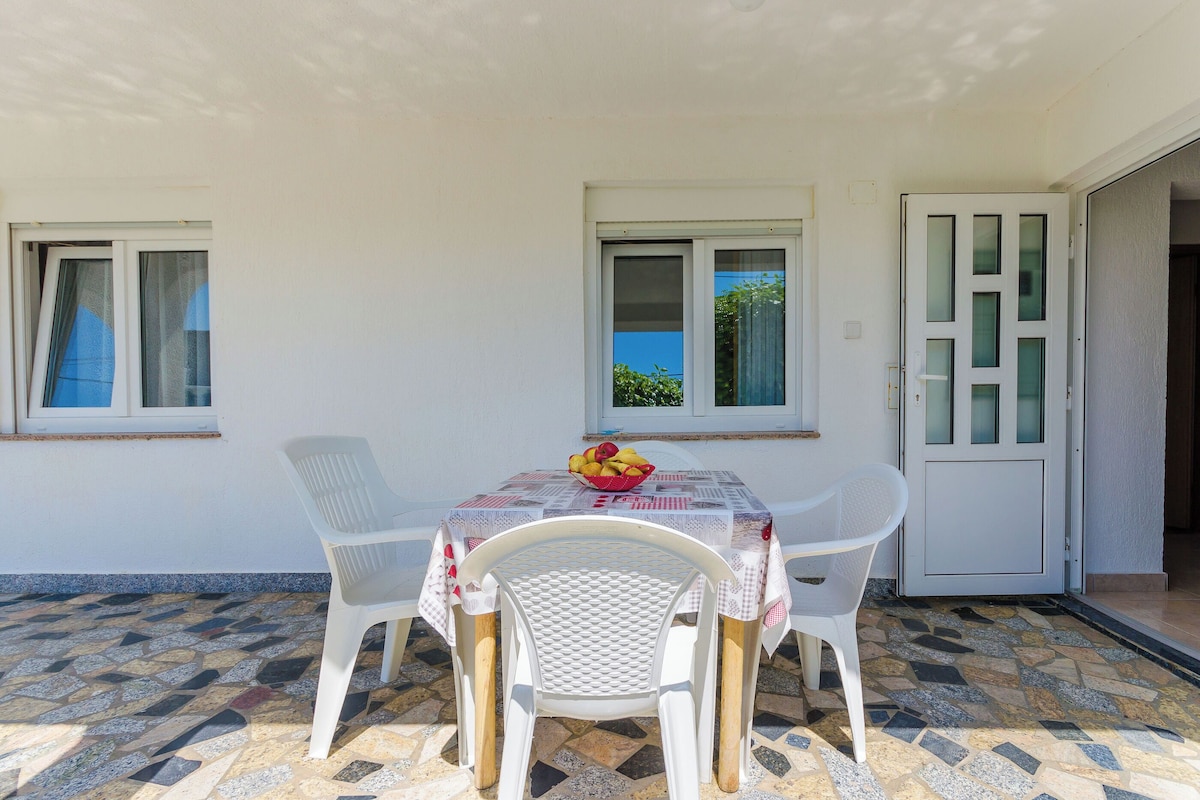 Uma pequena área de refeições com uma mesa, cadeiras, uma tigela de frutas e duas janelas com cortinas.