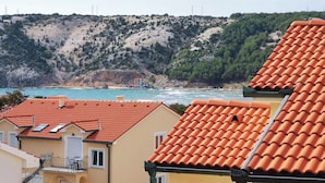 Uma vila costeira com casas de telhados em terracota, vista clara para o mar e um relevo montanhoso ao fundo.
