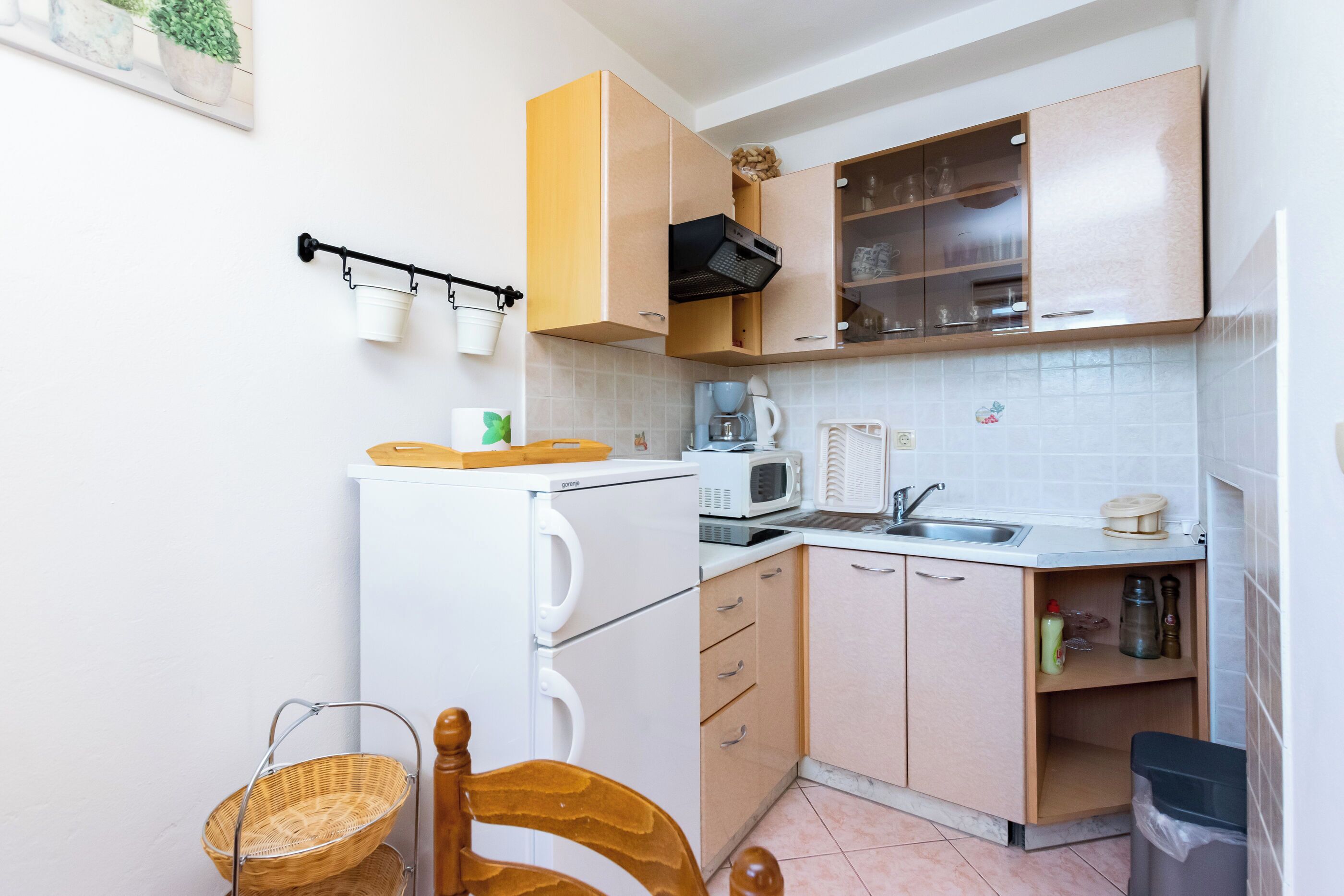 Uma cozinha compacta com eletrodomésticos brancos, armários de madeira e uma pequena lixeira.