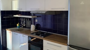 Uma cozinha moderna com armários brancos, geladeira de aço inoxidável e painel de azulejos pretos.