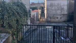 Pátio murado com um edifício, uma construção menor e vista para o mar.