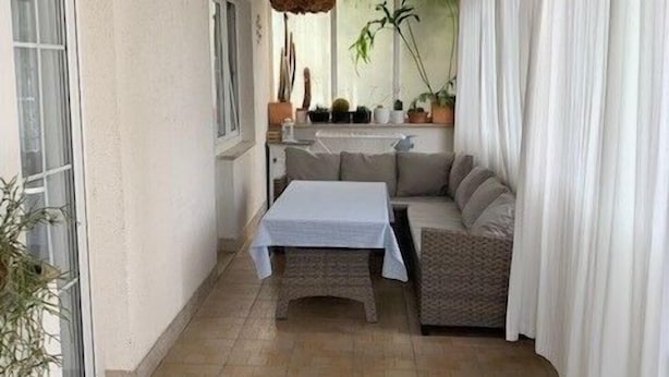 Um pátio ensolarado com mesa de pedra, assentos acolchoados e ventoinha no teto.
