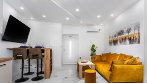 Quarto de hotel moderno com piso de mármore, sofá amarelo, mesa de jantar de madeira com cadeiras, TV de tela plana na parede e um quadro na parede.