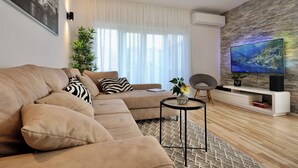 Uma sala de estar moderna com um sofá bege, uma mesinha de centro redonda, uma TV em uma parede de tijolos e um console branco.