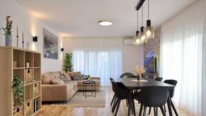 Uma sala de estar moderna com um sofá, mesa de jantar e cadeiras. Há uma estante com objetos decorativos e uma pintura na parede.