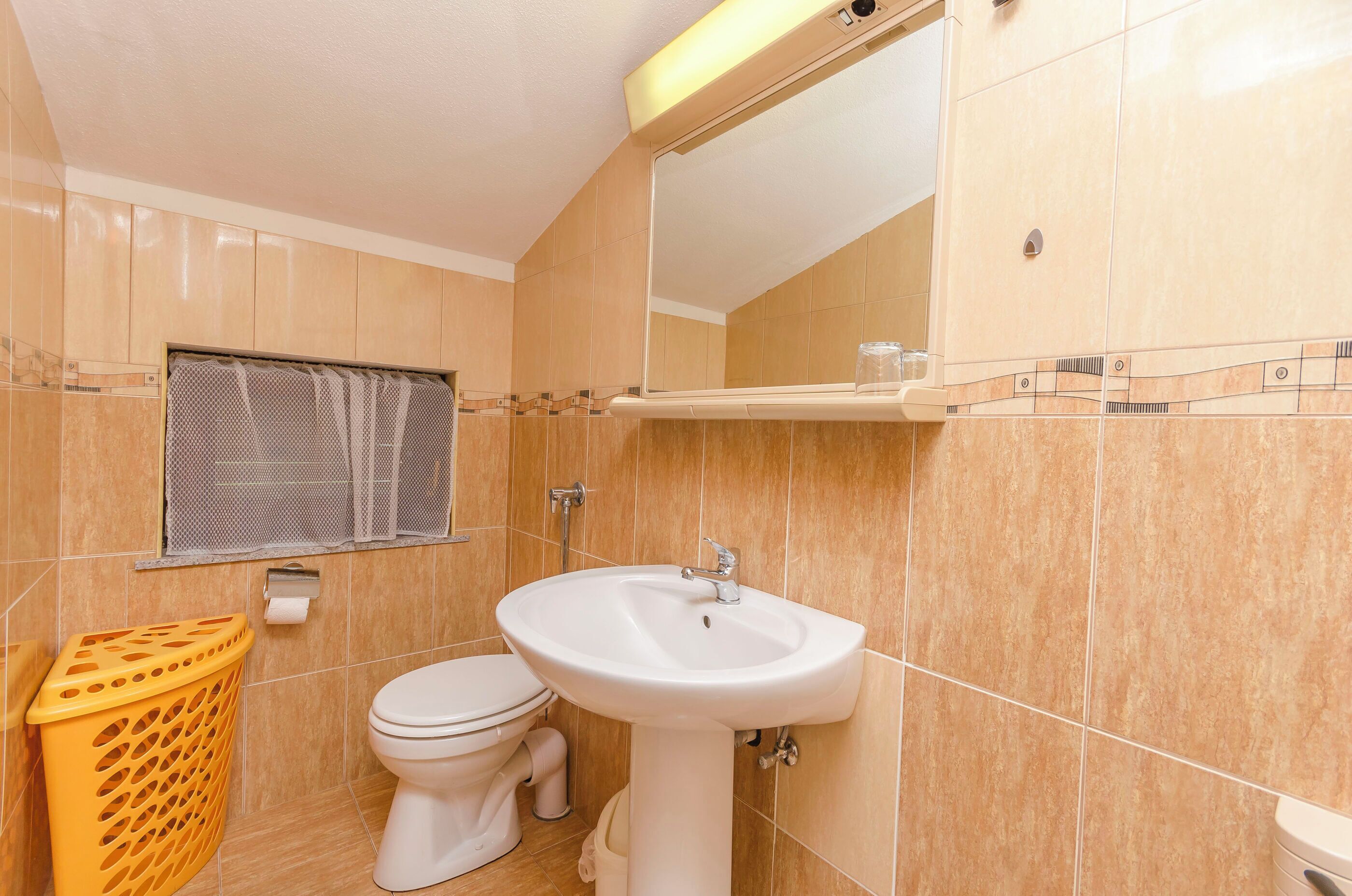 Casa de banho com lavatório branco, sanita e cesto de roupa amarelo.