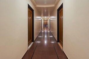 Corredor comprido e estreito, com portas de madeira em ambos os lados e chão de azulejos brilhantes.