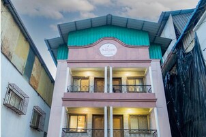 Um edifício com uma placa que diz "The Sangam". Possui várias varandas com grades de metal e janelas com persianas.