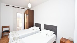 Quarto de hotel com duas camas de solteiro, uma cadeira de madeira, uma pequena mesa de cabeceira e uma janela com cortinas.