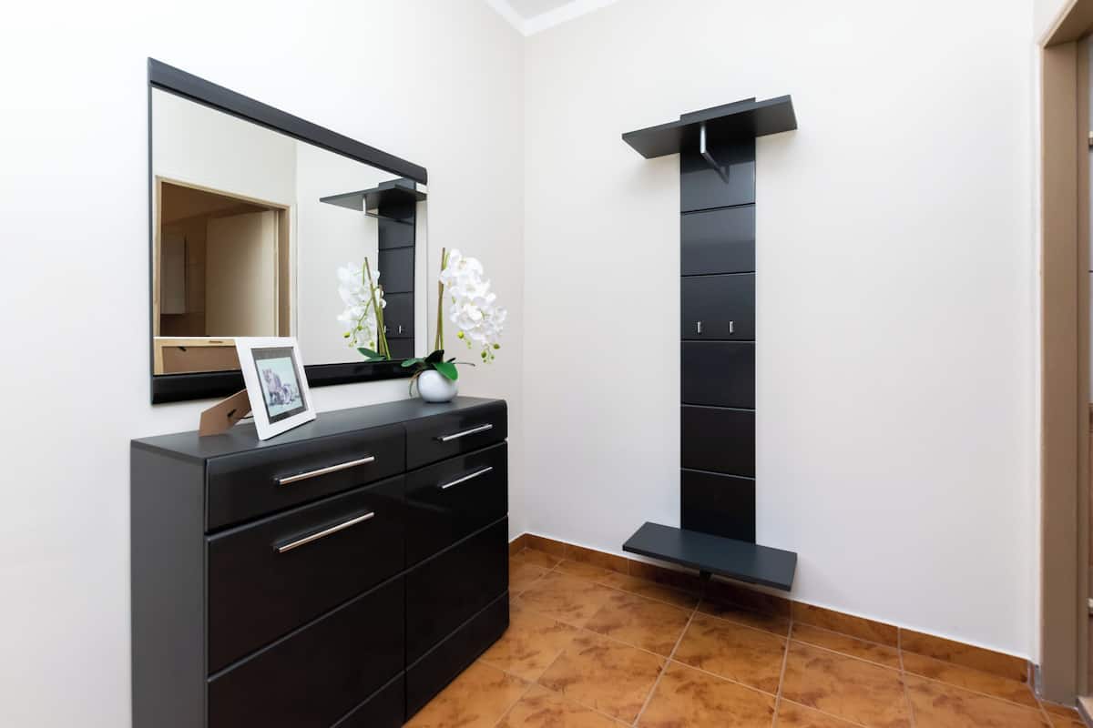 Quarto moderno com cômoda preta, espelho, orquídea branca e estante preta.